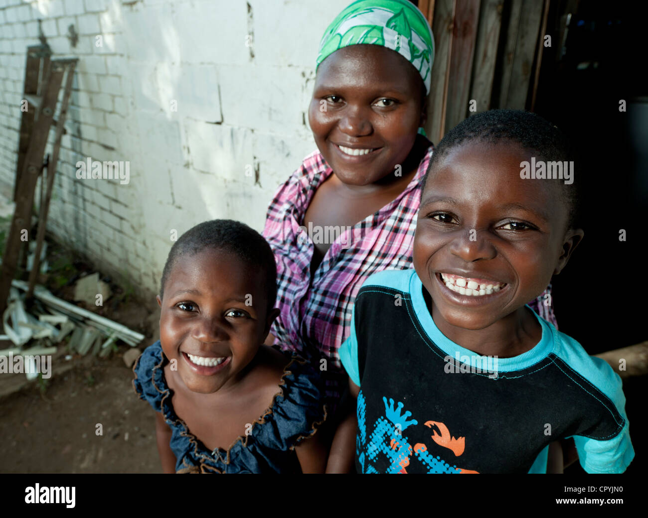 An African woman and her two children stand outside their rural home ...