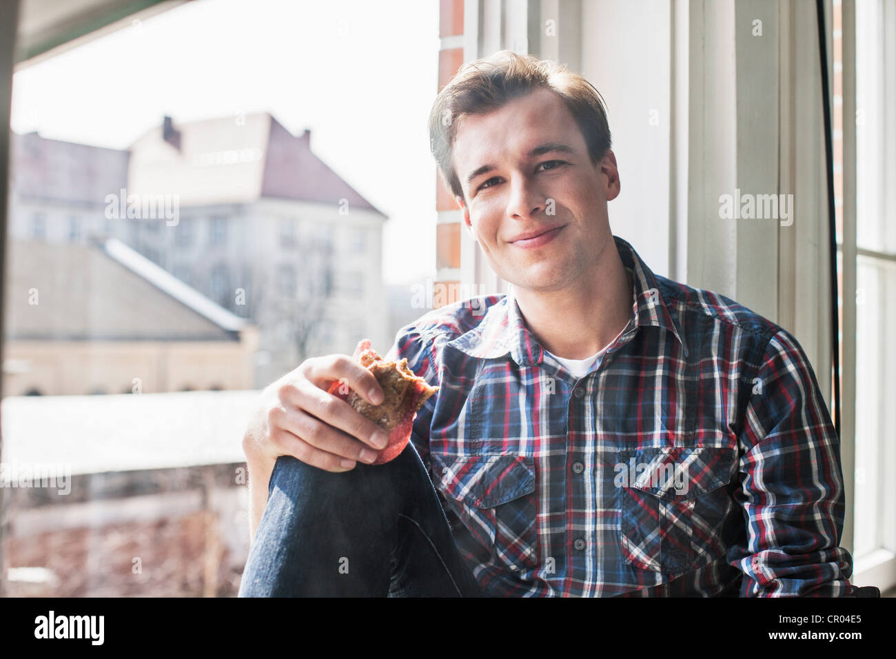 Smiling man eating sandwich in window Stock Photo - Alamy