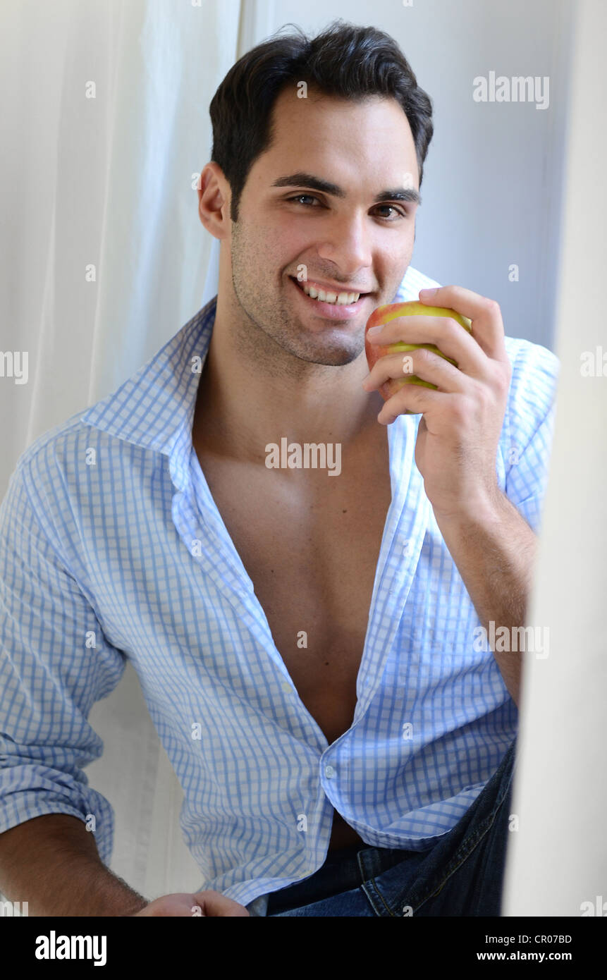 Young man sitting on a window sill eating an apple Stock Photo - Alamy