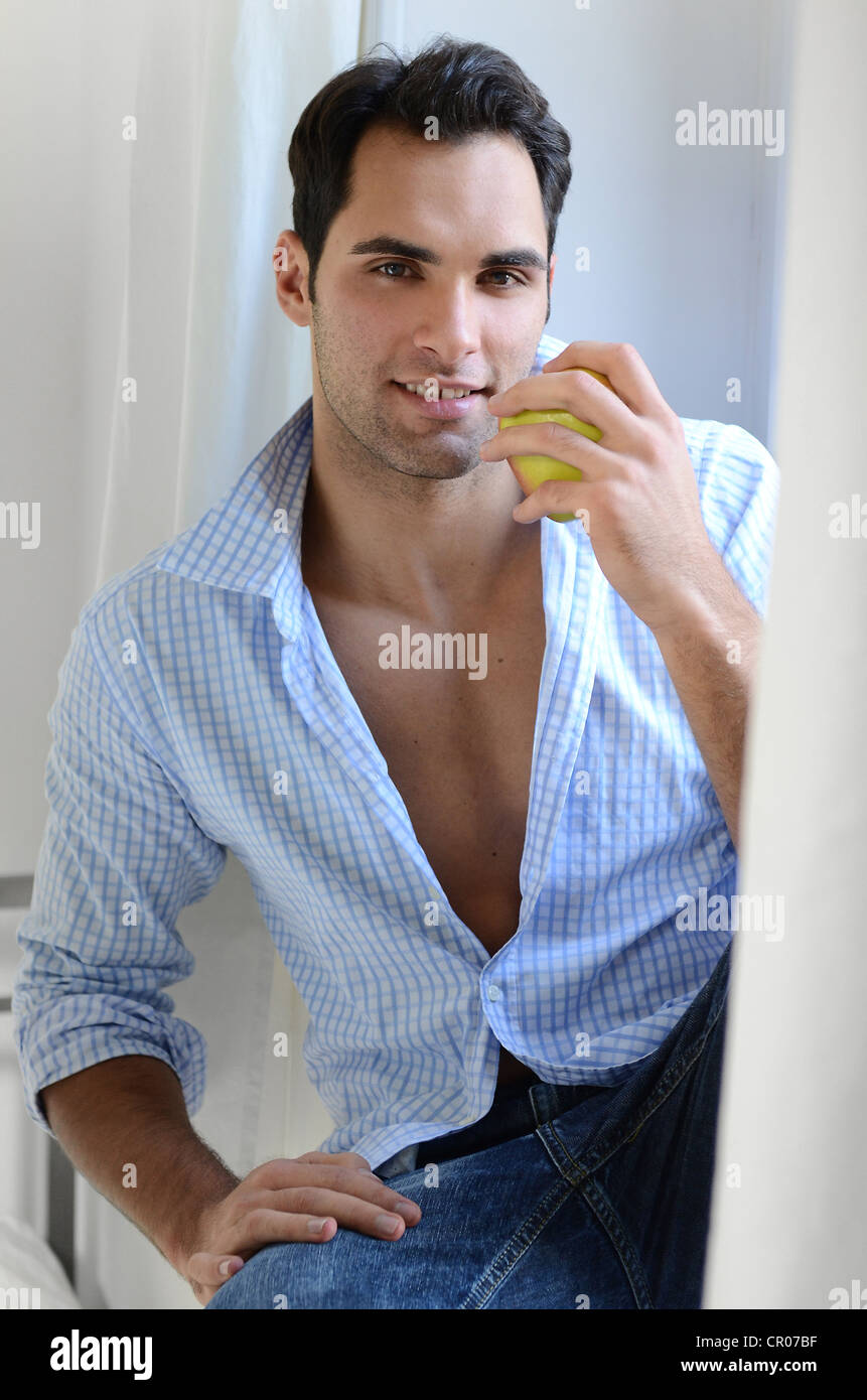 Young man sitting on a window sill eating an apple Stock Photo - Alamy