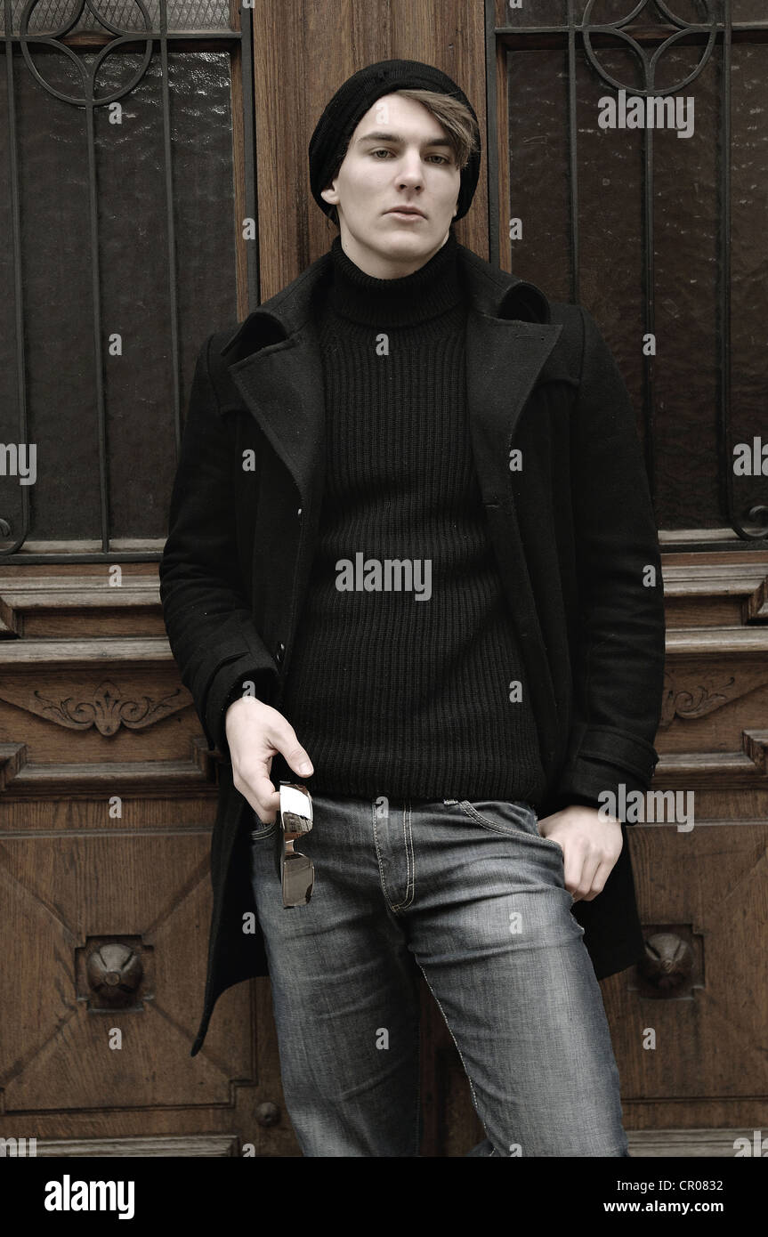 Young man wearing winter clothes, standing in front of a front door ...