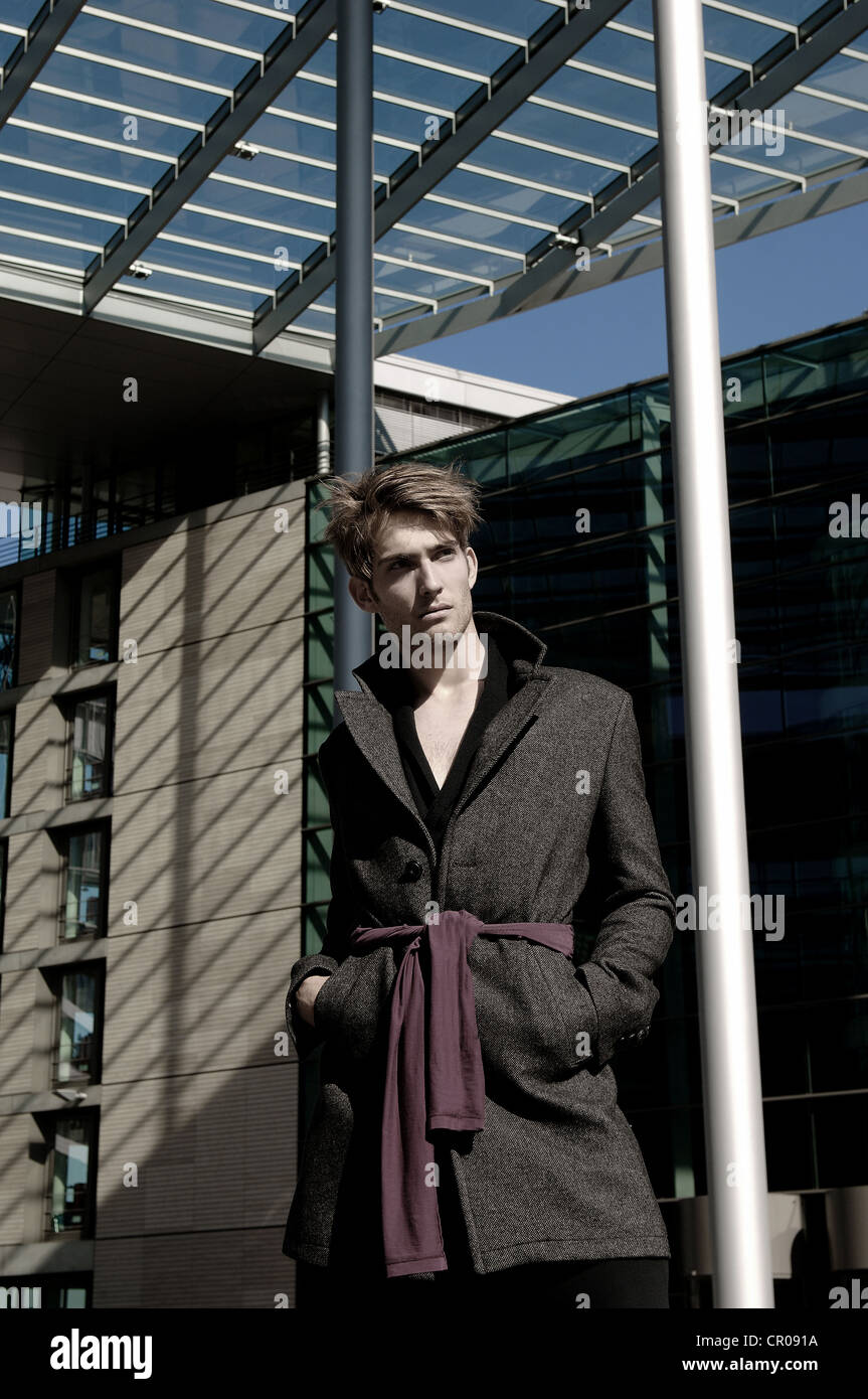 Young man wearing an overcoat in front of modern architecture, fashion ...