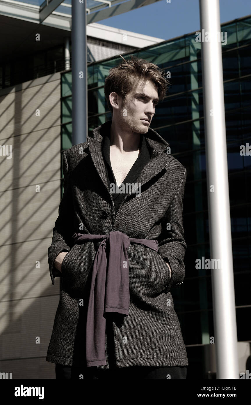 Young man wearing an overcoat in front of modern architecture, fashion ...
