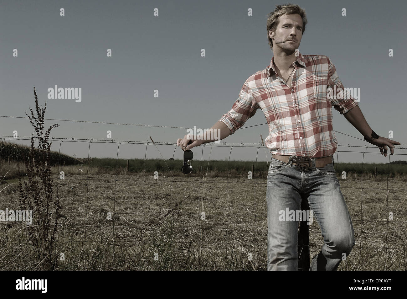Cowboy leaning against a wire fence Stock Photo - Alamy