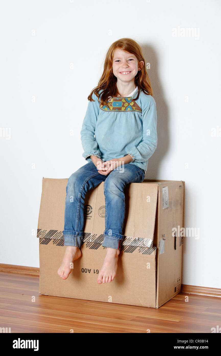Girl sitting on a cardboard box, packing case Stock Photo - Alamy