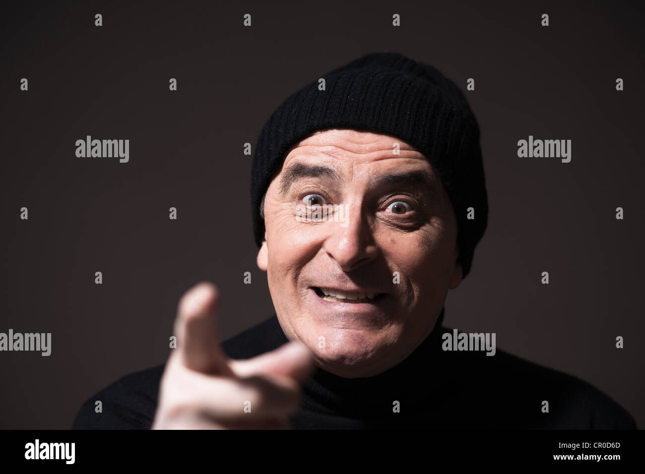 Elderly man wearing a black woollen hat pointing towards the front ...