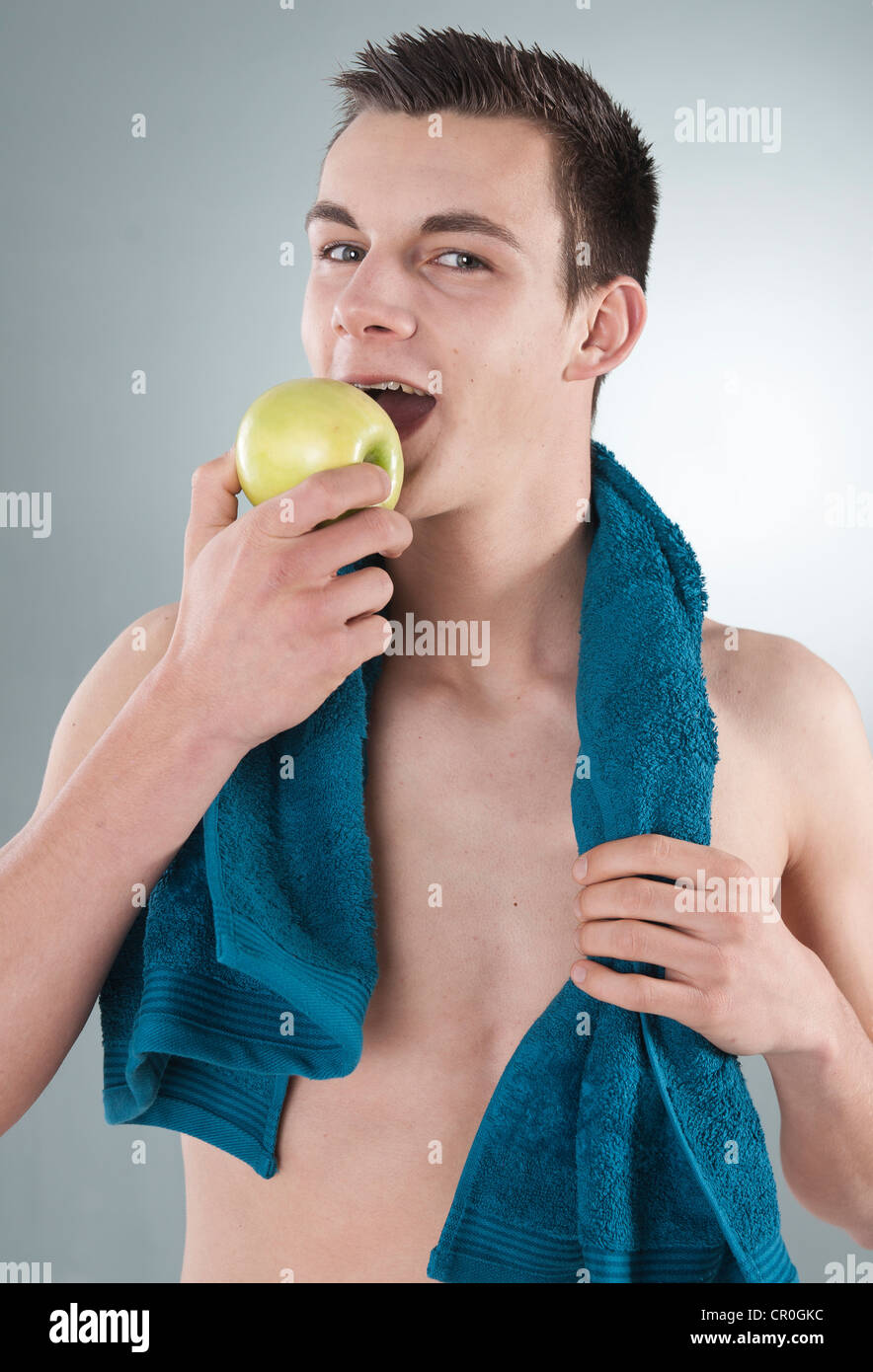Young man with a bare torso and a towel around his shoulders biting ...