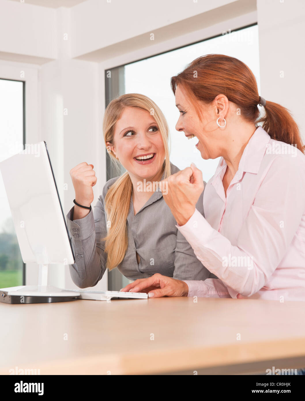 Two women cheering while sitting in front of a computer Stock Photo - Alamy