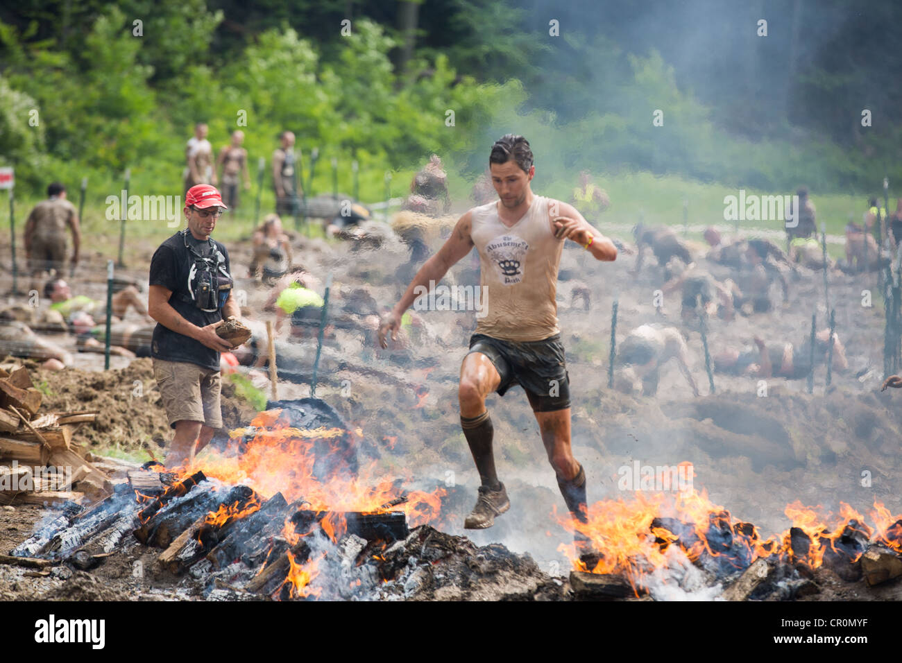Young male jumping fire, last obstacle of a challenging sprint trail ...