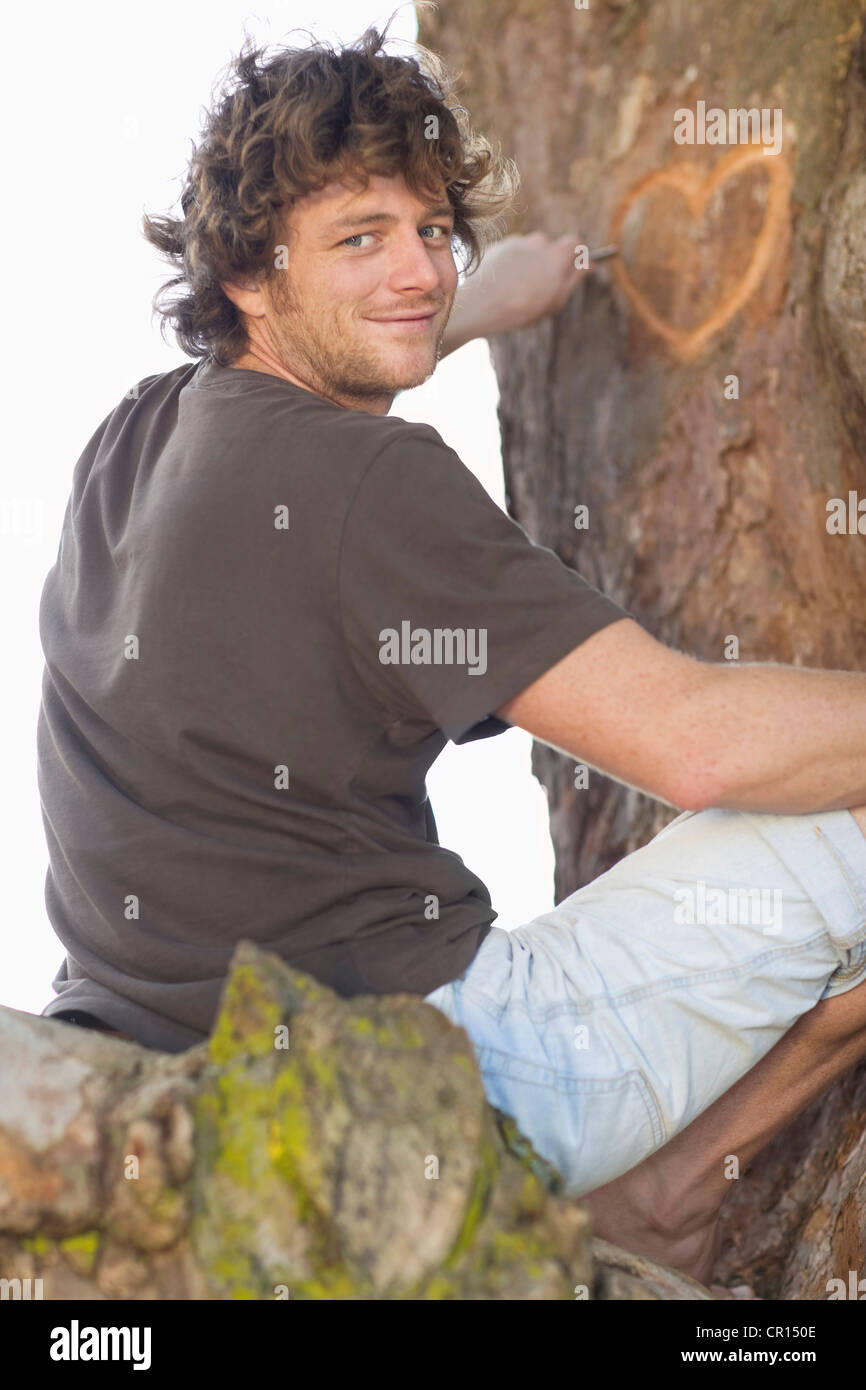 Smiling man carving heart in tree Stock Photo - Alamy
