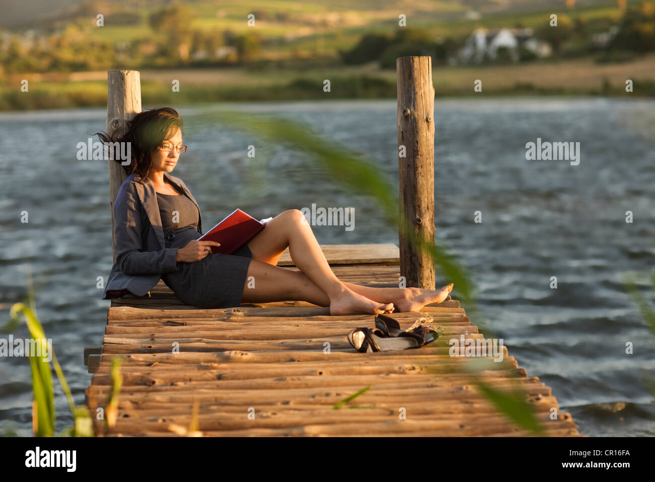 Woman reading book on dock Stock Photo - Alamy