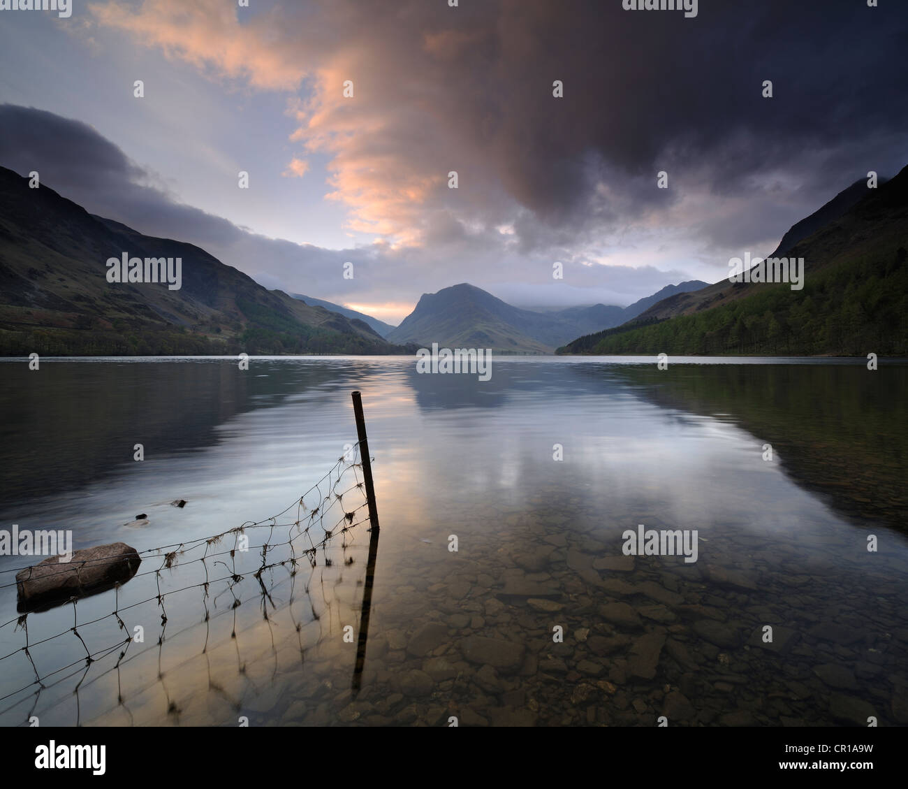 A colourful sunrise reflected in the still waters of Buttermere in the ...