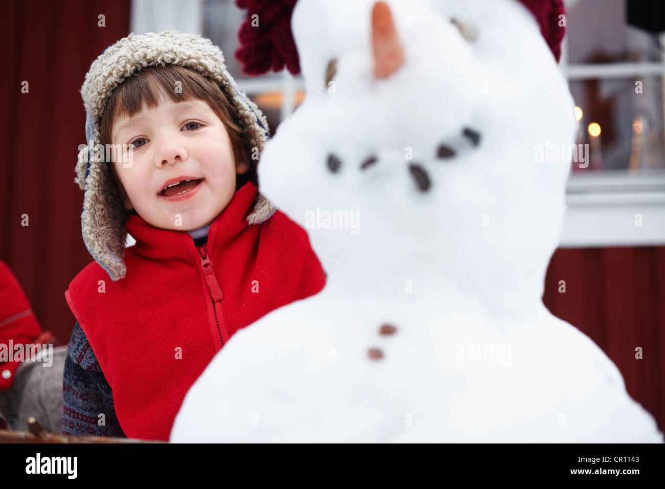 Boy standing behind snowman Stock Photo - Alamy