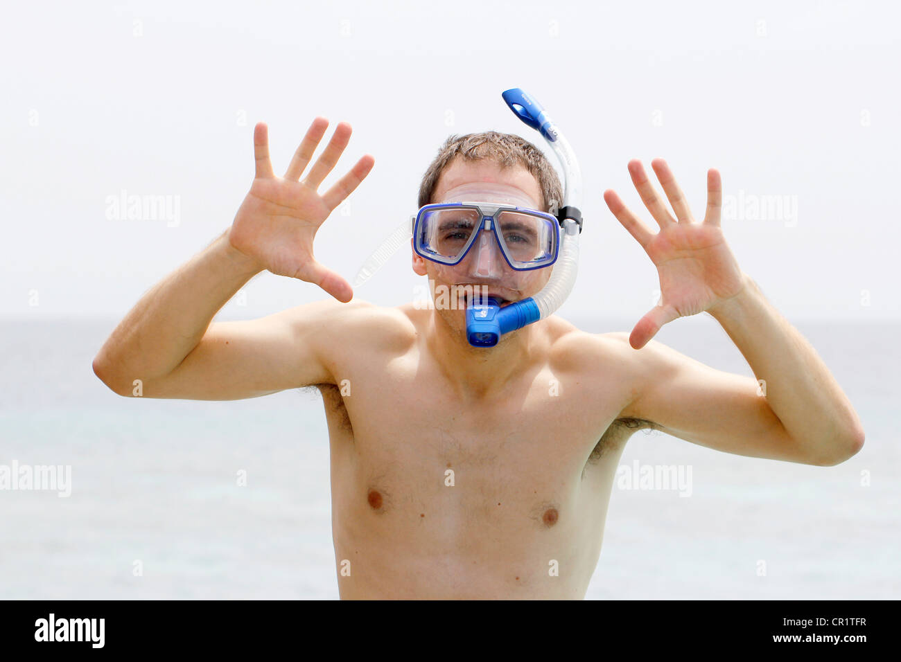 Man wearing diving goggles and snorkel, ready to dive, showing hands ...