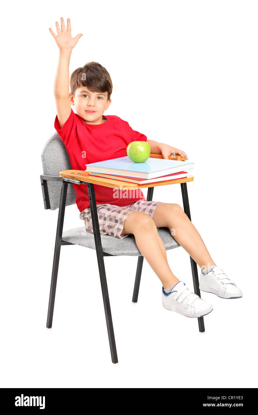 A studio shot of a schoolboy seated in a chair raising his hand ...