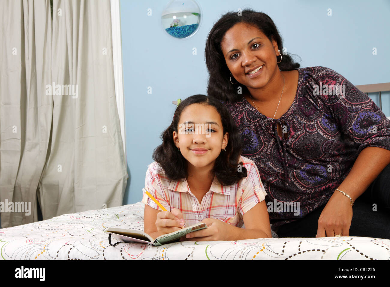 Girl writing in journal on her bed with mom Stock Photo - Alamy