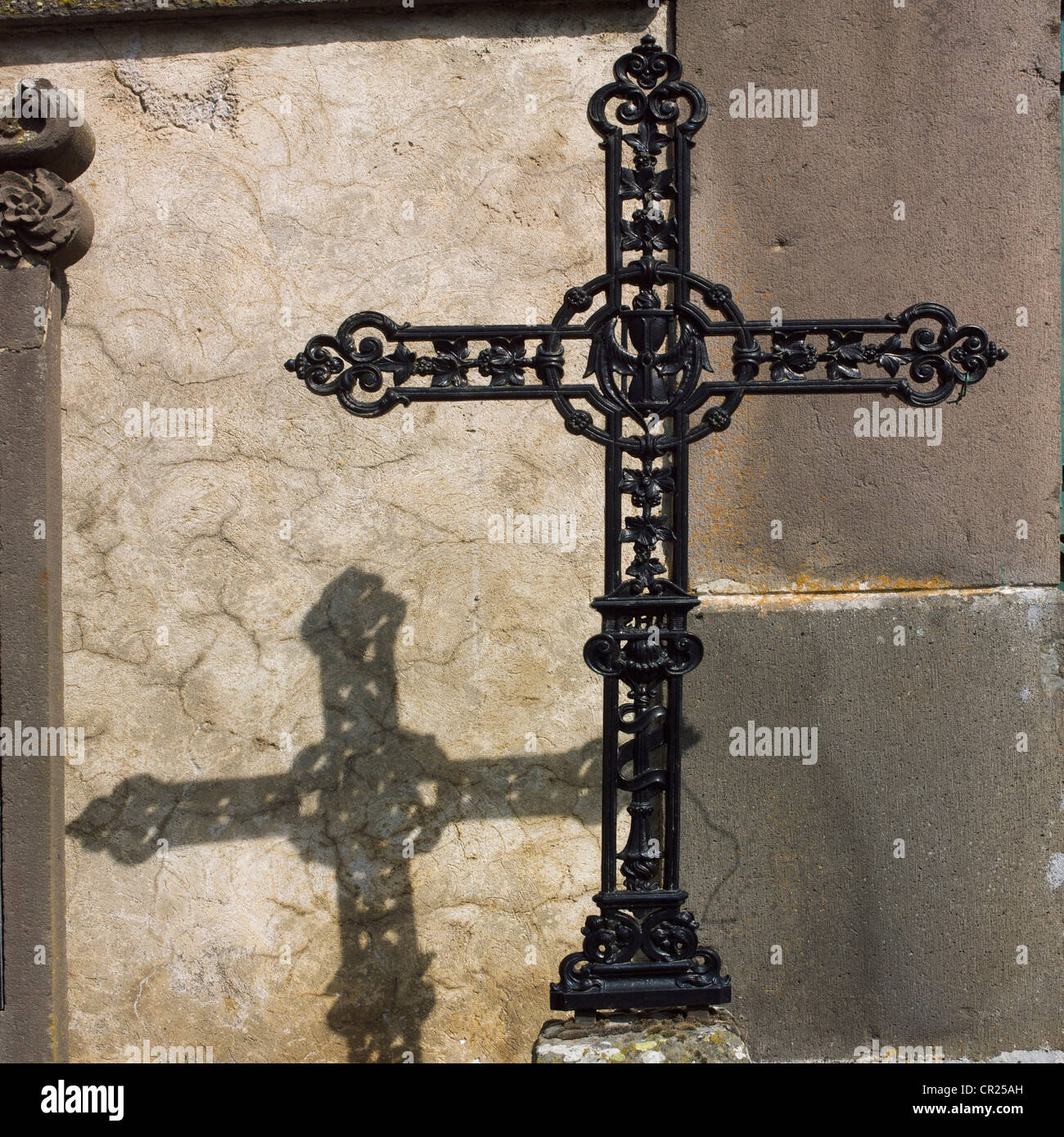 Intricate iron cross casting shadow on textured wall at cemetery ...