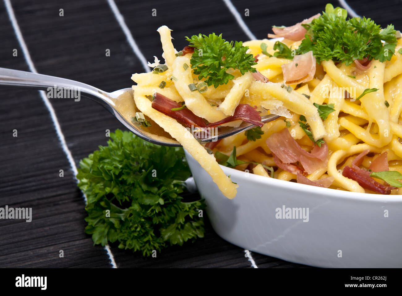 Portion of Cheese Spaetzle in a bowl with portion on fork (on black ...
