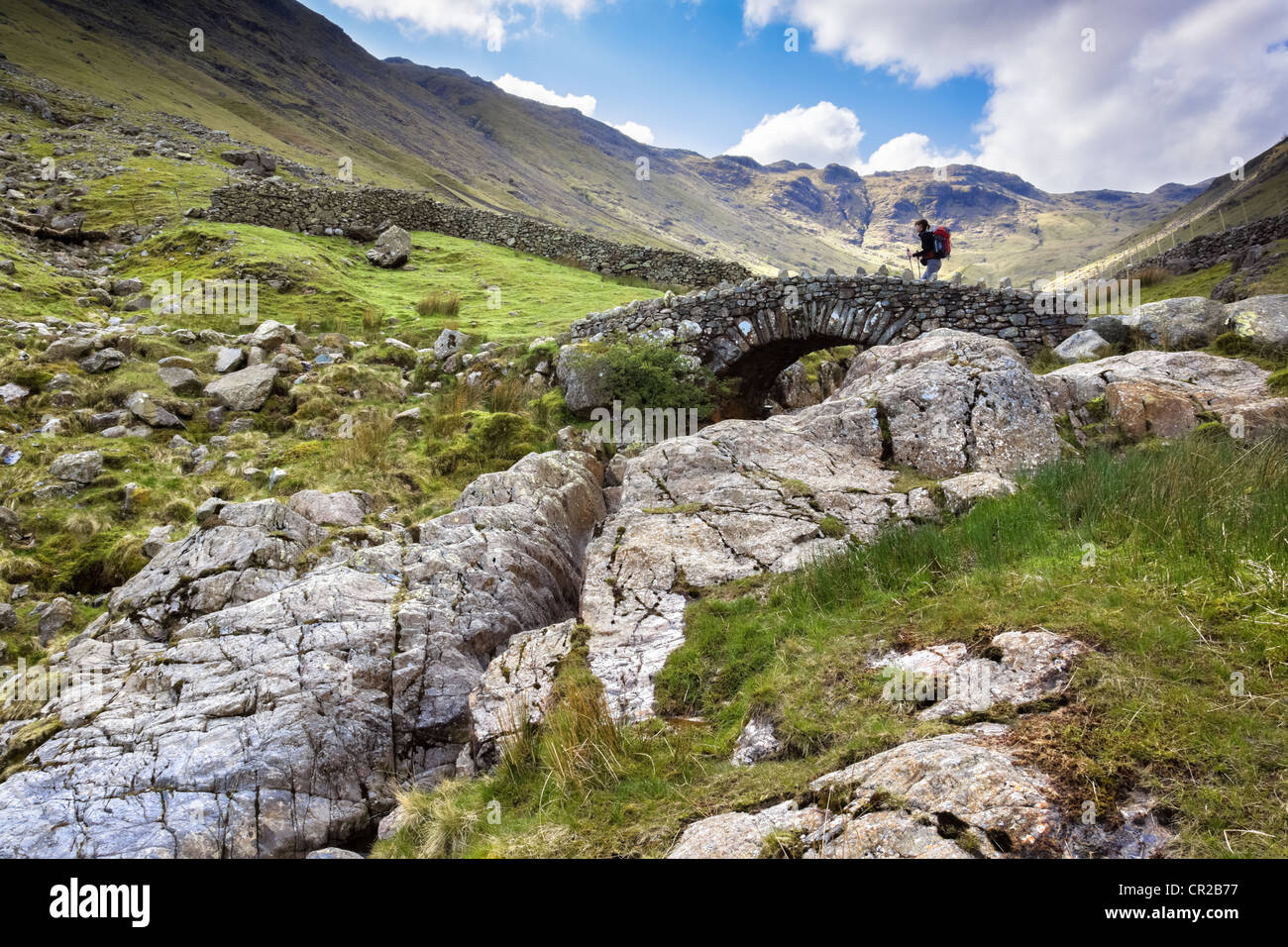 A hiker crosses Stockley Bridge on a bright spring day from Seathwaite ...
