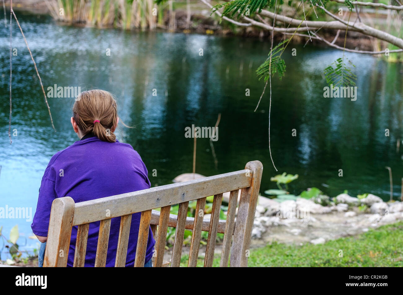 Lady on bench looking thoughtfully at a tranquil, tropical pond Stock ...