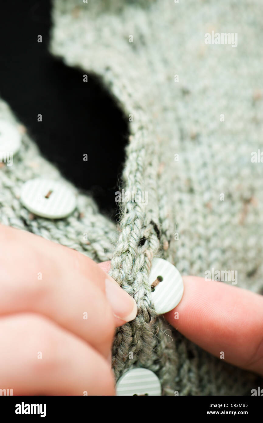 Abstract close up of man doing up buttons on a hand-knitted jumper ...