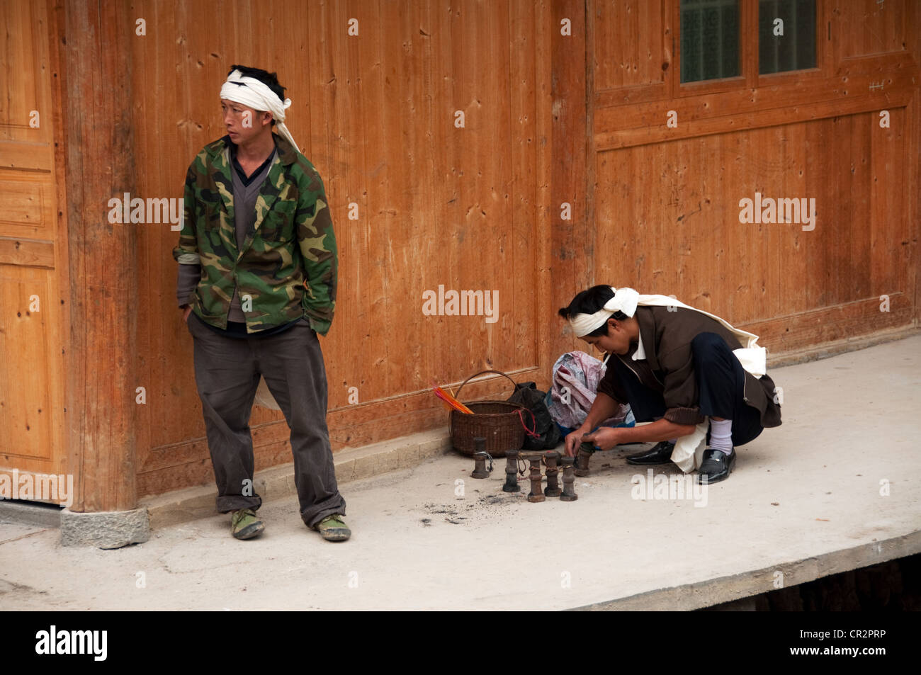 Two Dong men with white scarves preparing fireworks at a funeral rite ...