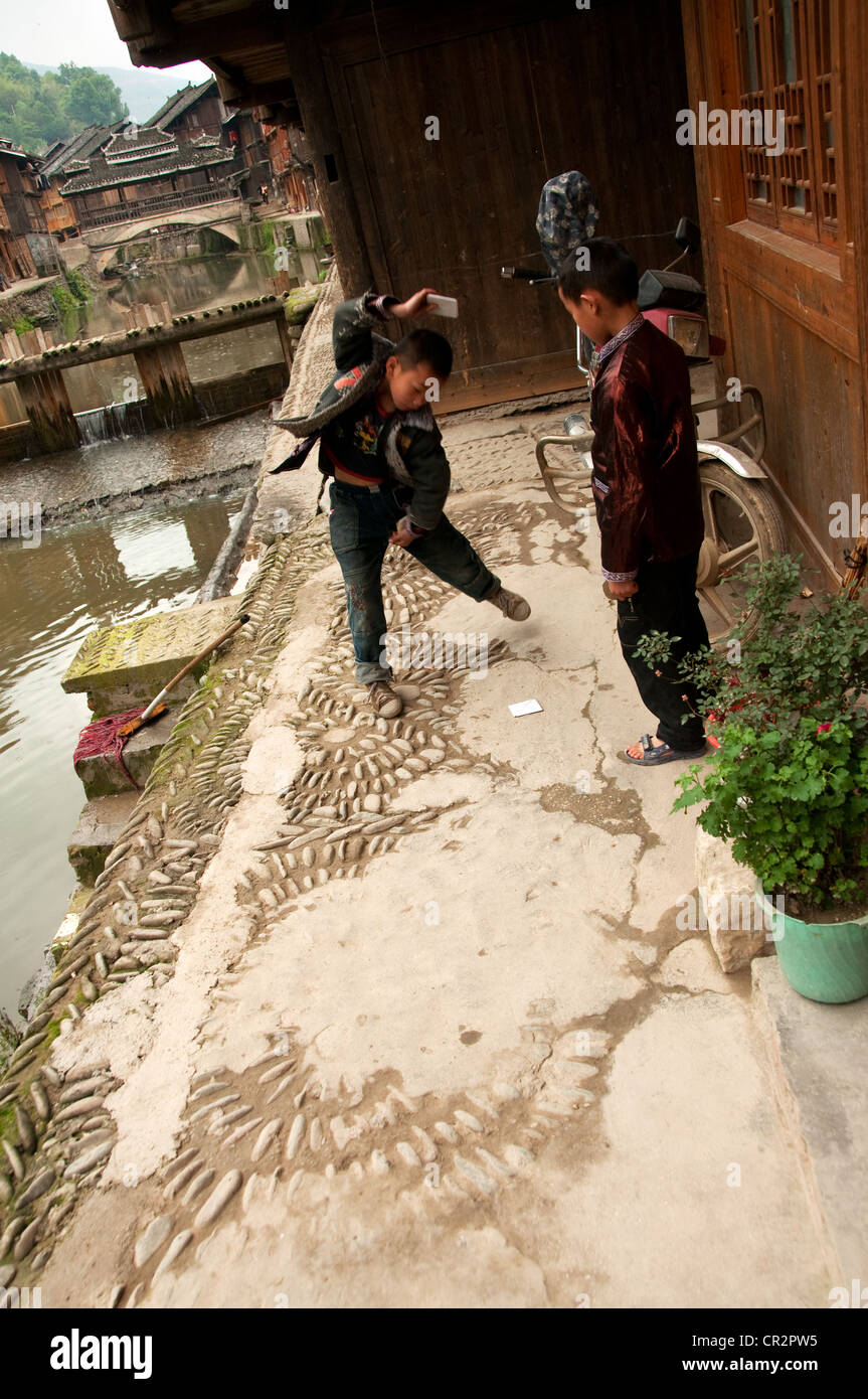 Two Chinese Dong kids playing with cards on a narrow lane near a stream ...
