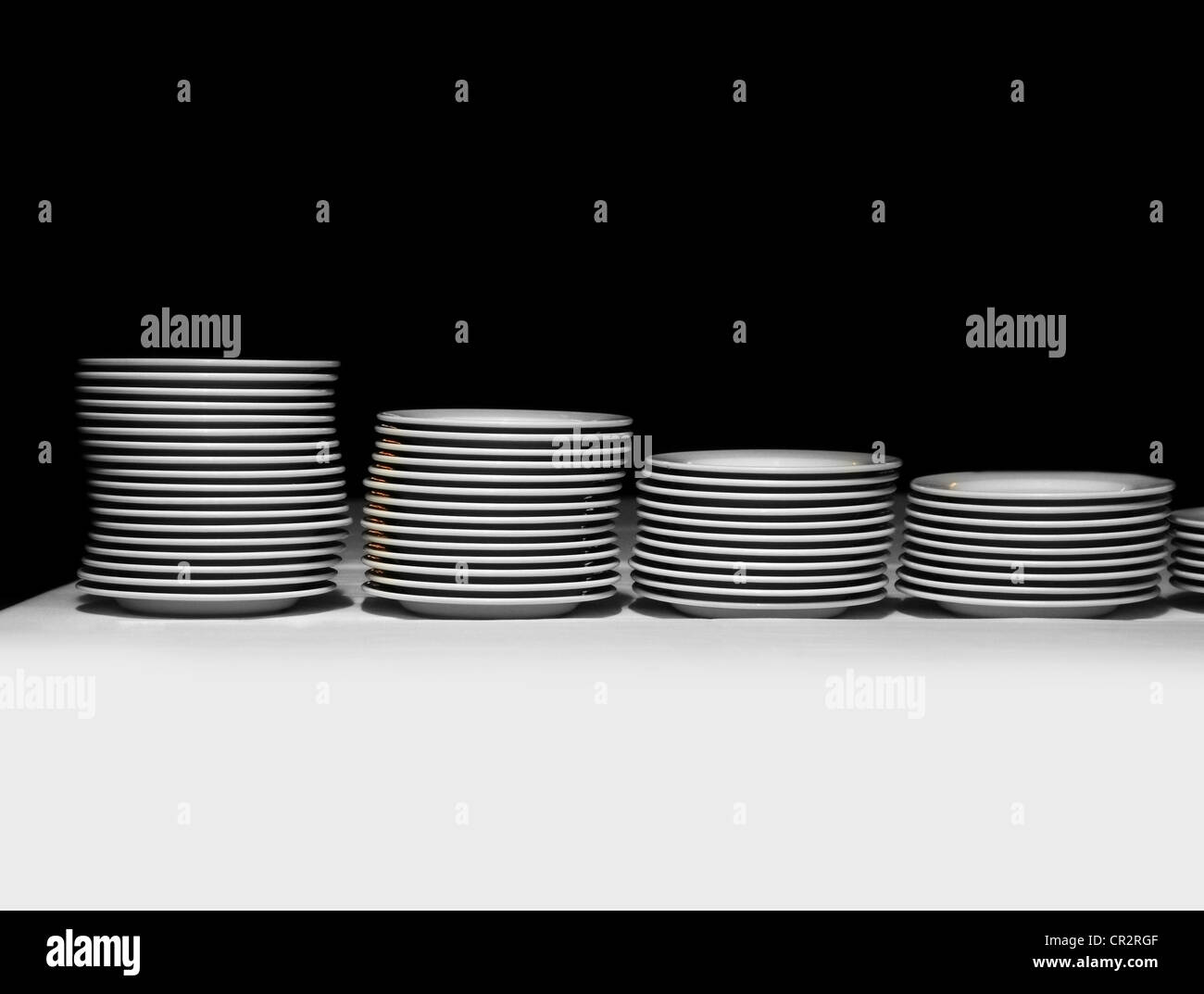 Pile of white plates on a black background Stock Photo - Alamy