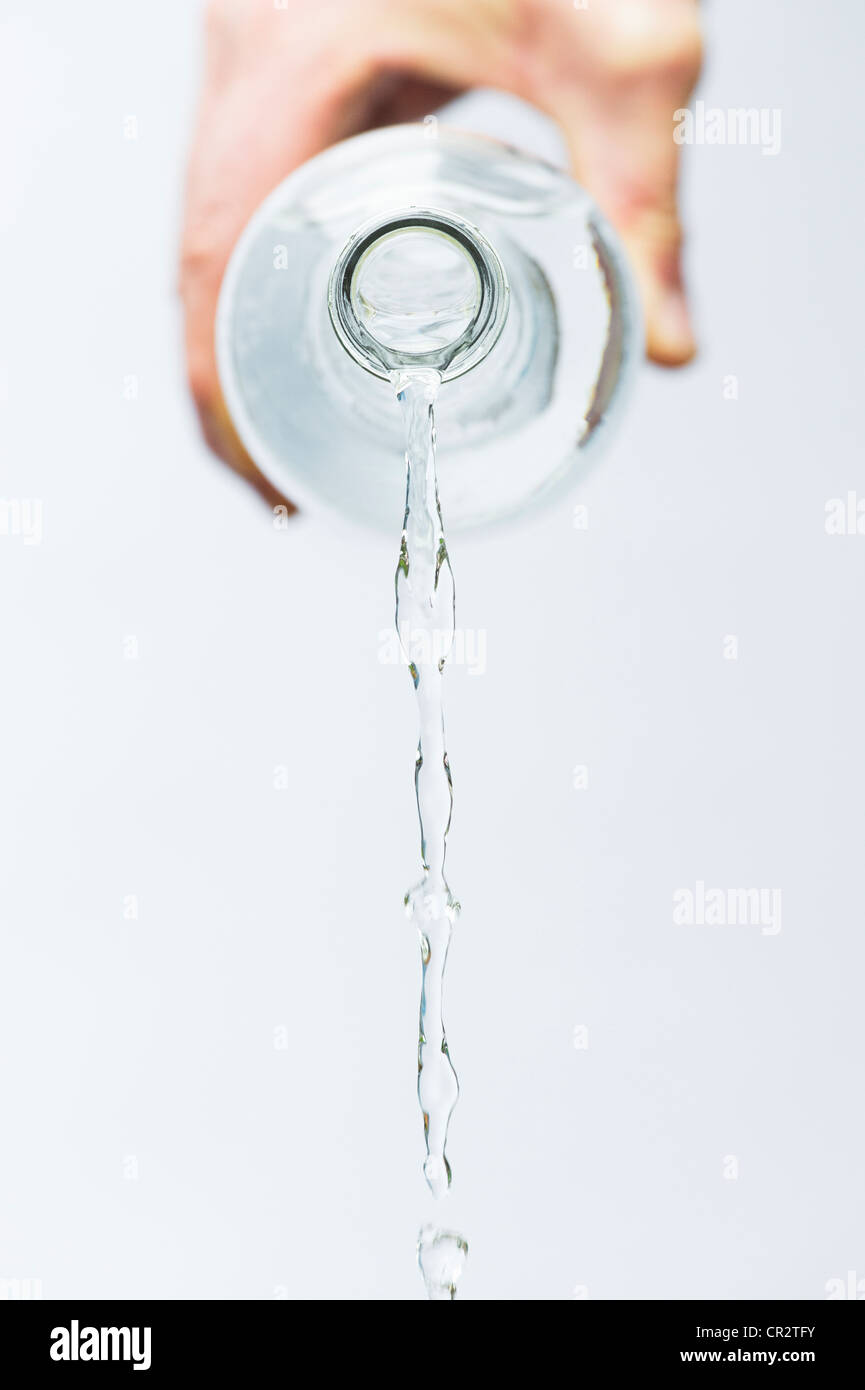 Hand pouring mineral water from a glass bottle against white background Stock Photo - Alamy