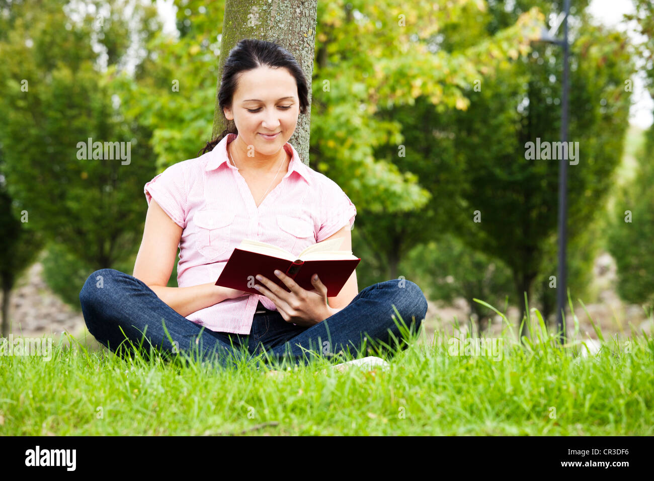 Young woman leaning against a tree, reading a book Stock Photo - Alamy