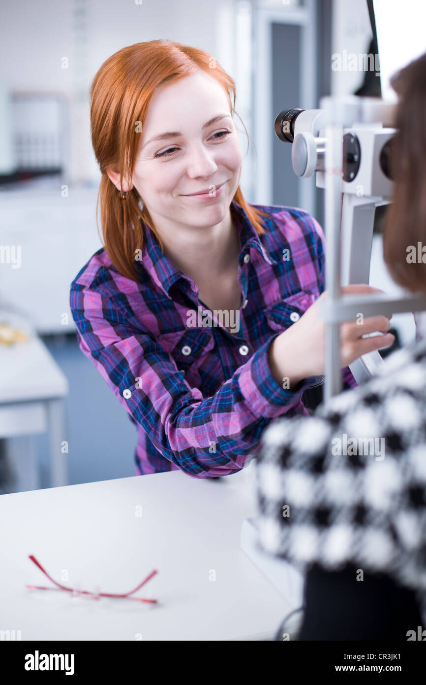 optometry concept - pretty young woman having her eyes examined by an ...