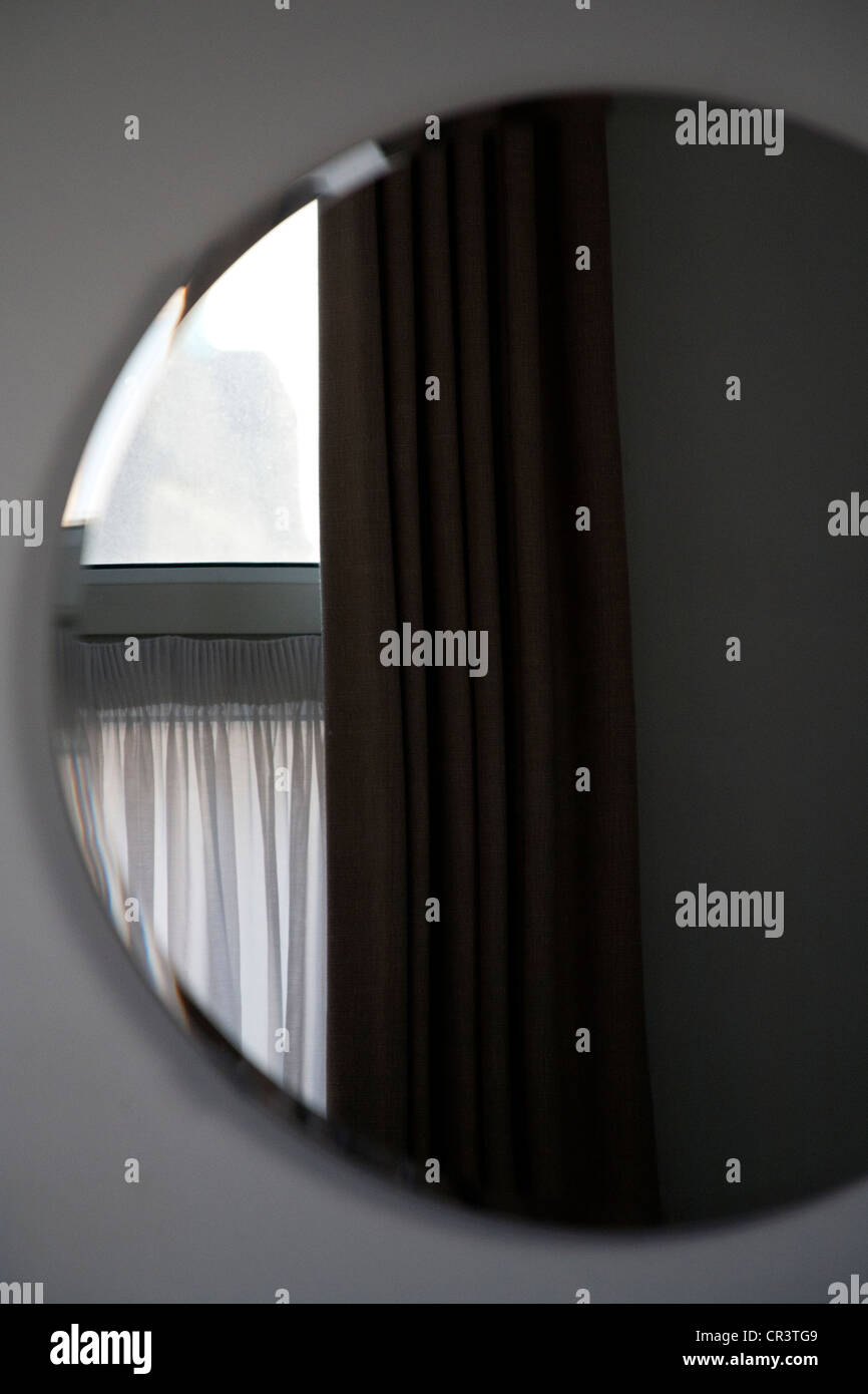 Curtain and window reflected in a round mirror on a hotel room wall ...