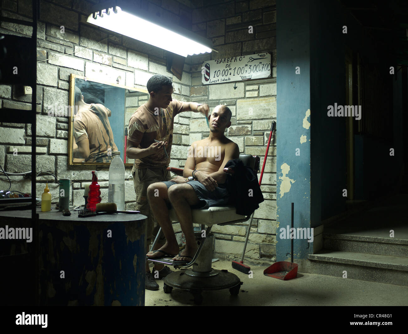 Barber cutting the hair of a Cubans man under fluorescent light in the ...