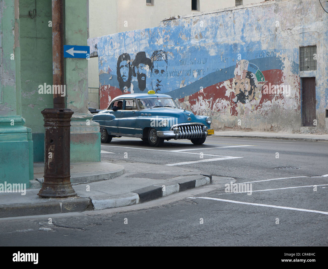 American vintage car driving along a wall with paintings of Fidel ...