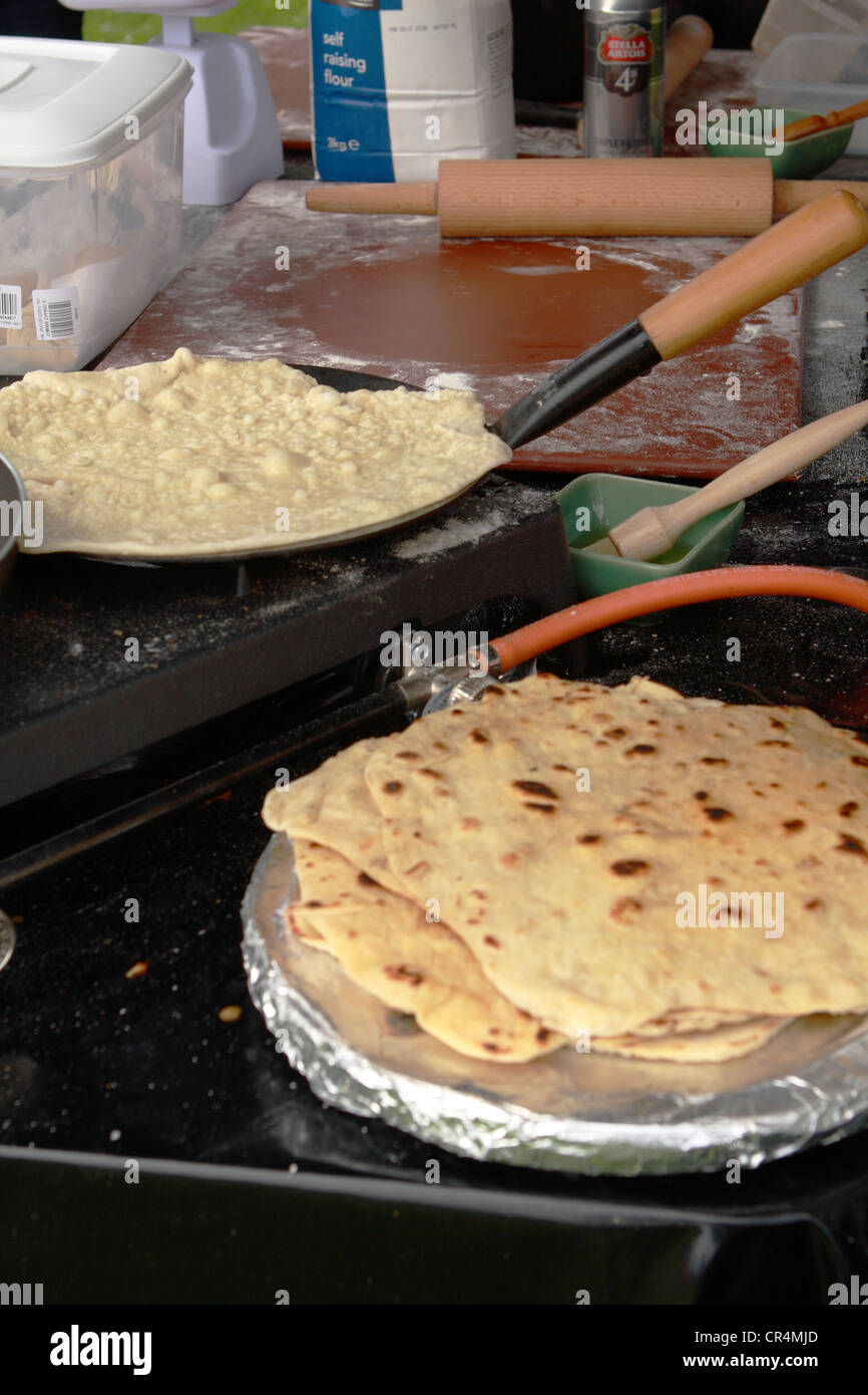 A small pile of rotis next to a roti being cooked on a portable gas ...