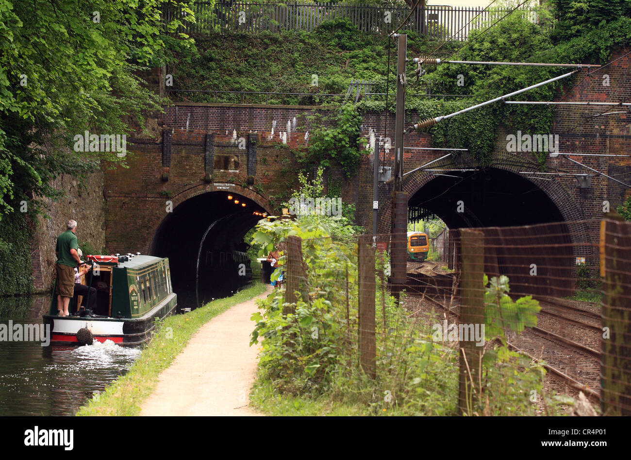 a bridge crossing a railway and canal with a boat and train approaching ...