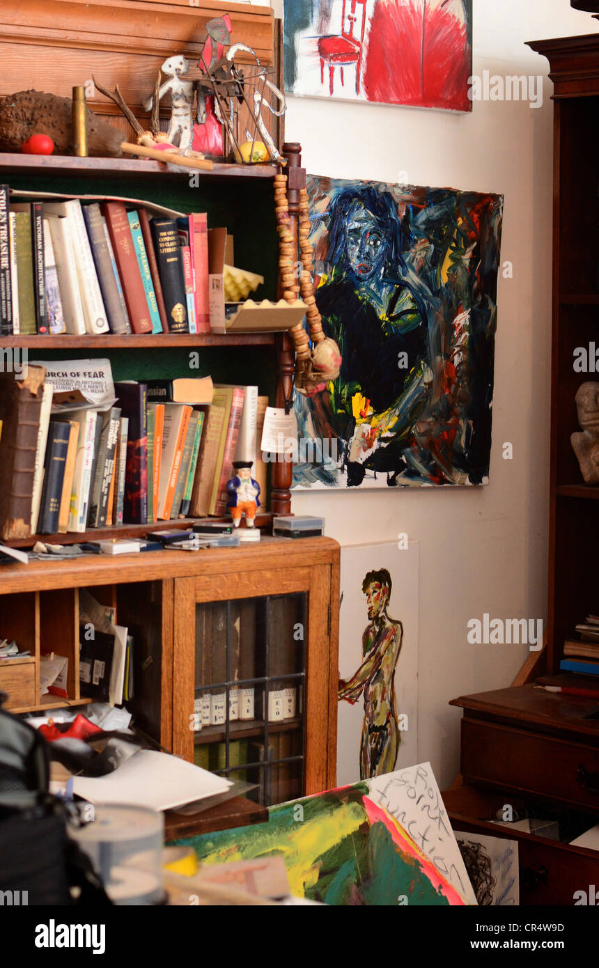 A messy artist's studio with many paintings books and other ...