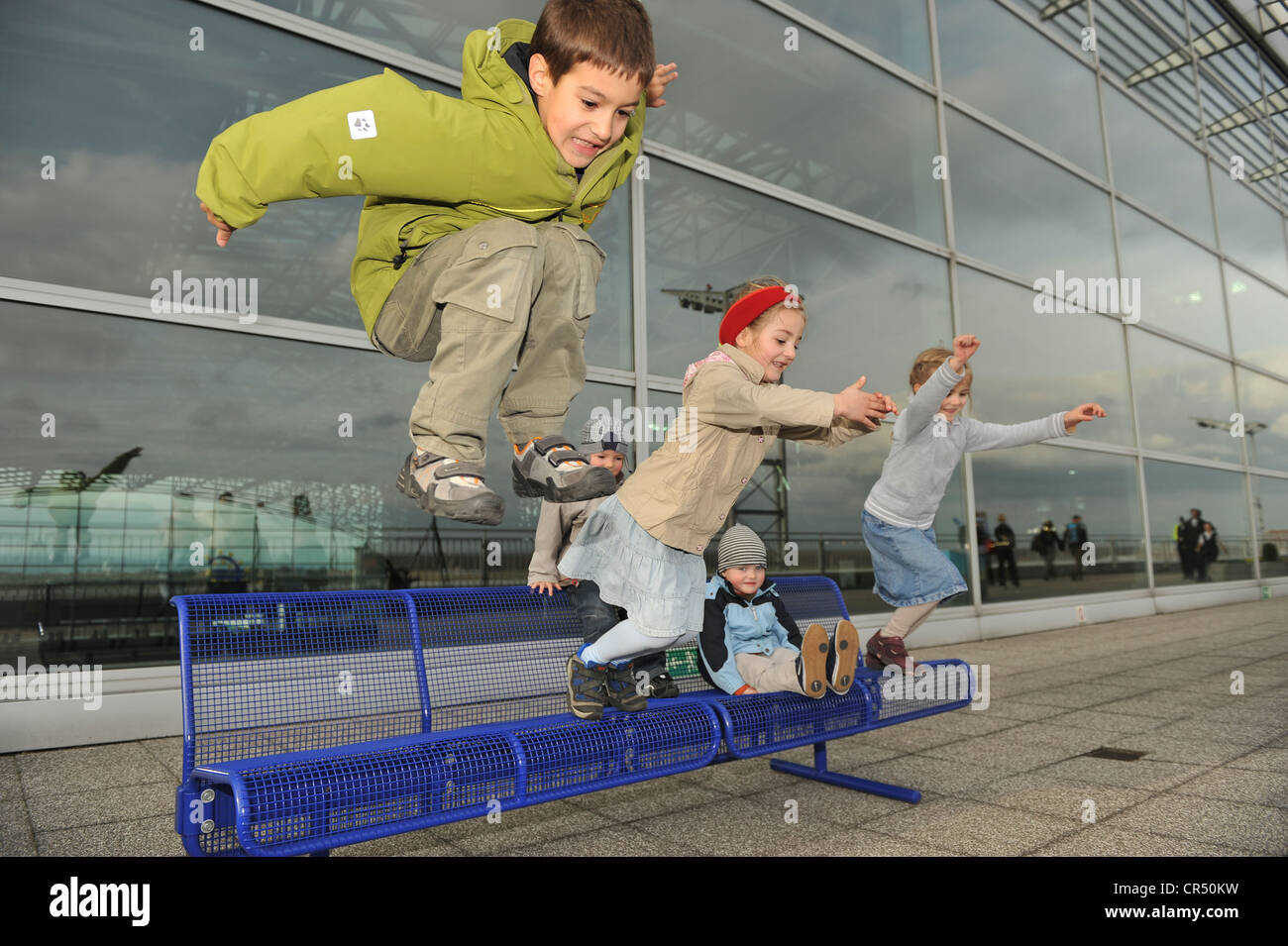 Children, between 3 and 7 years, jumping together from a bench at the ...