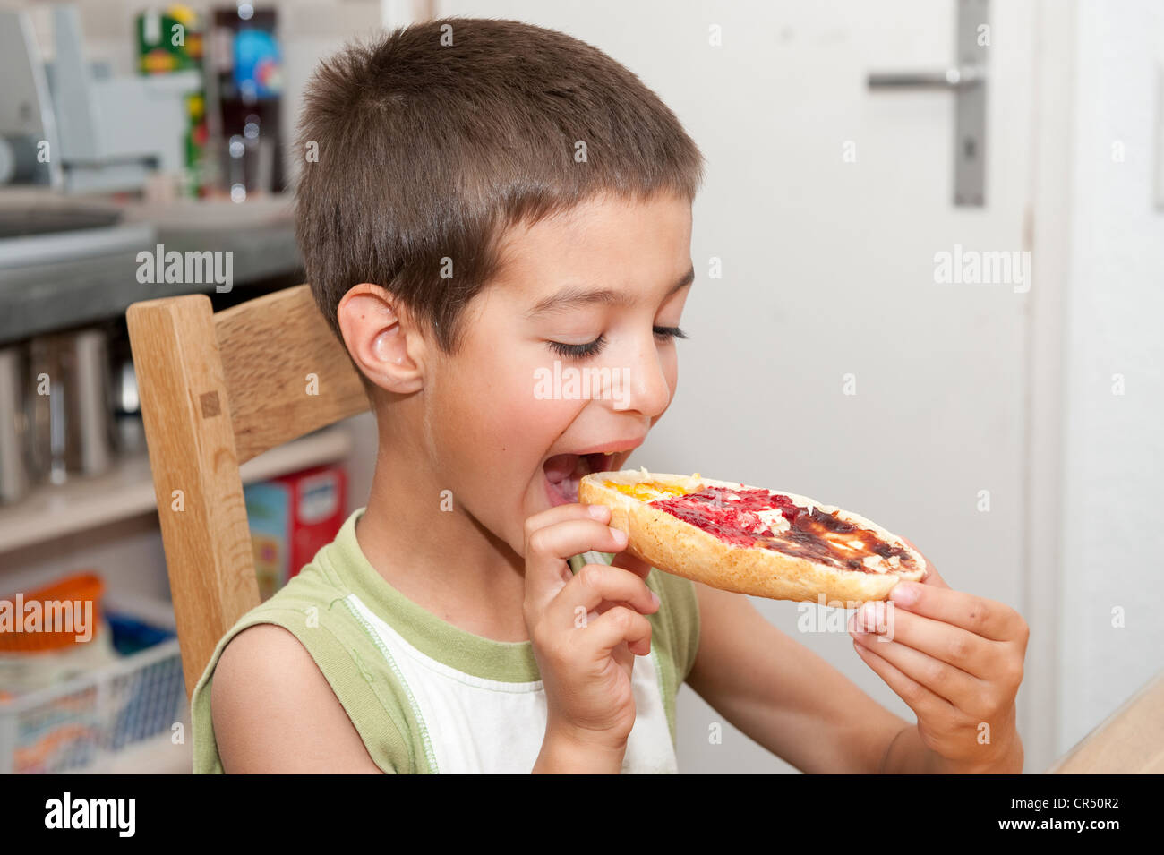 Boy, 7 years, biting into a bun with various jams Stock Photo - Alamy