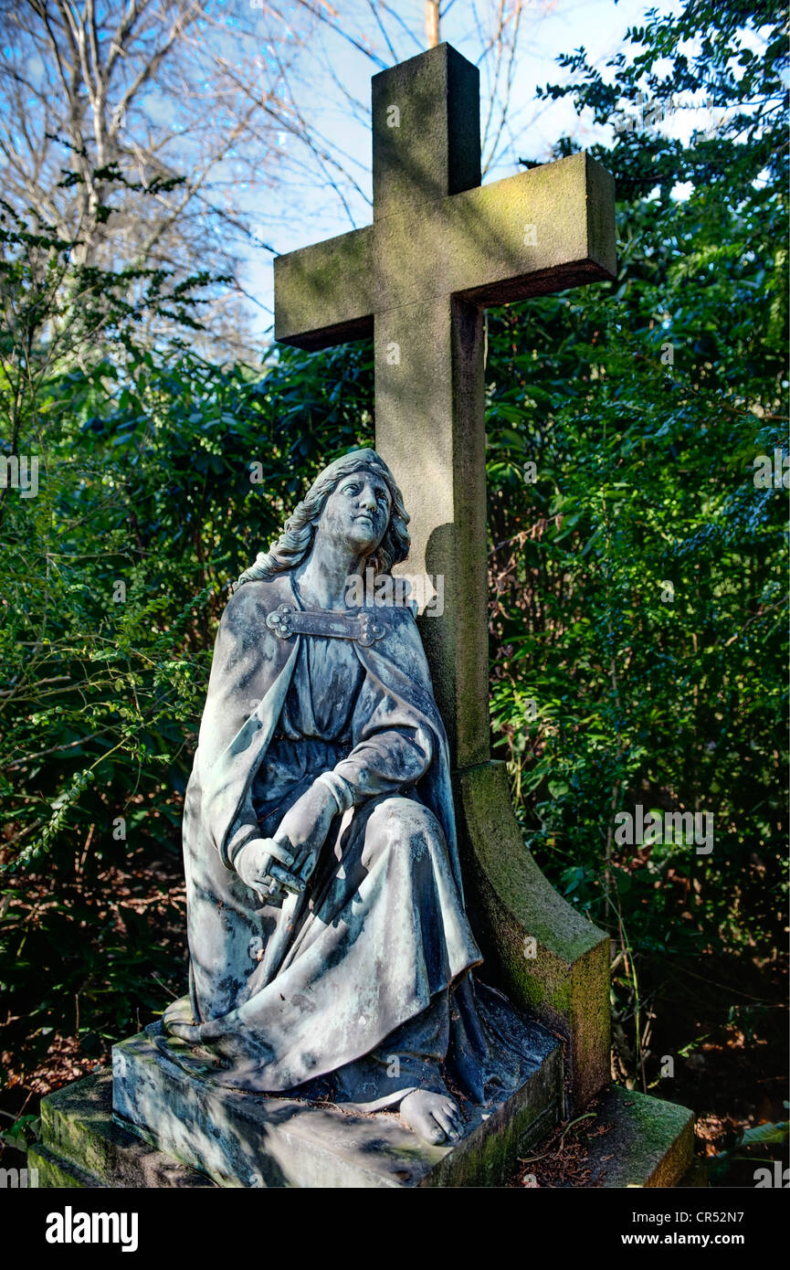 Historical gravestone with a statue and a cross at Ohlsdorf Cemetery in ...