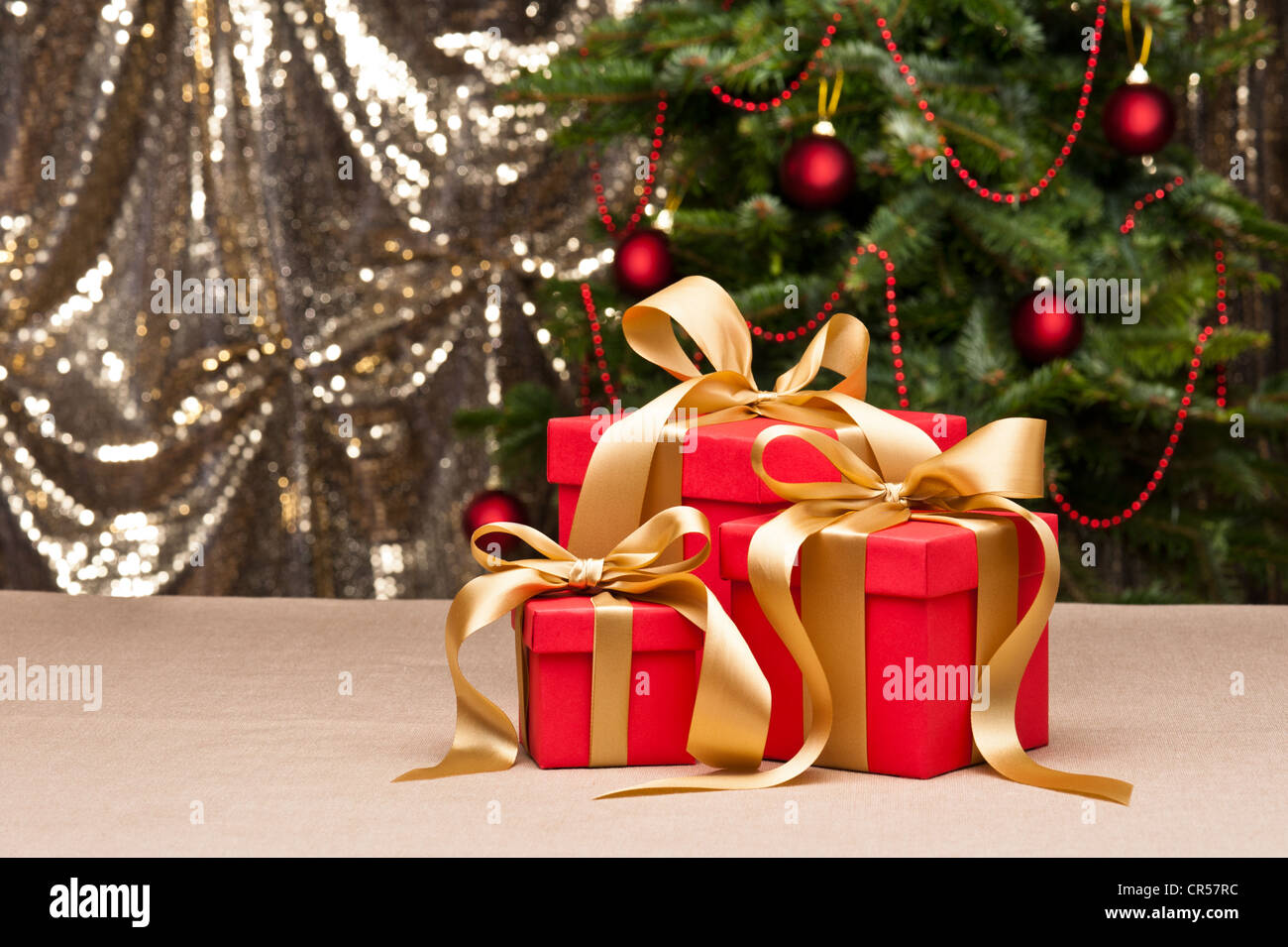 Three presents with gold ribbon, in front of a Christmas tree Stock ...