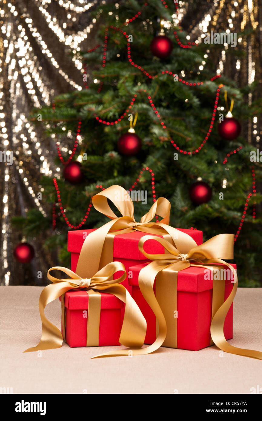 Three presents with gold ribbon, in front of a Christmas tree Stock ...