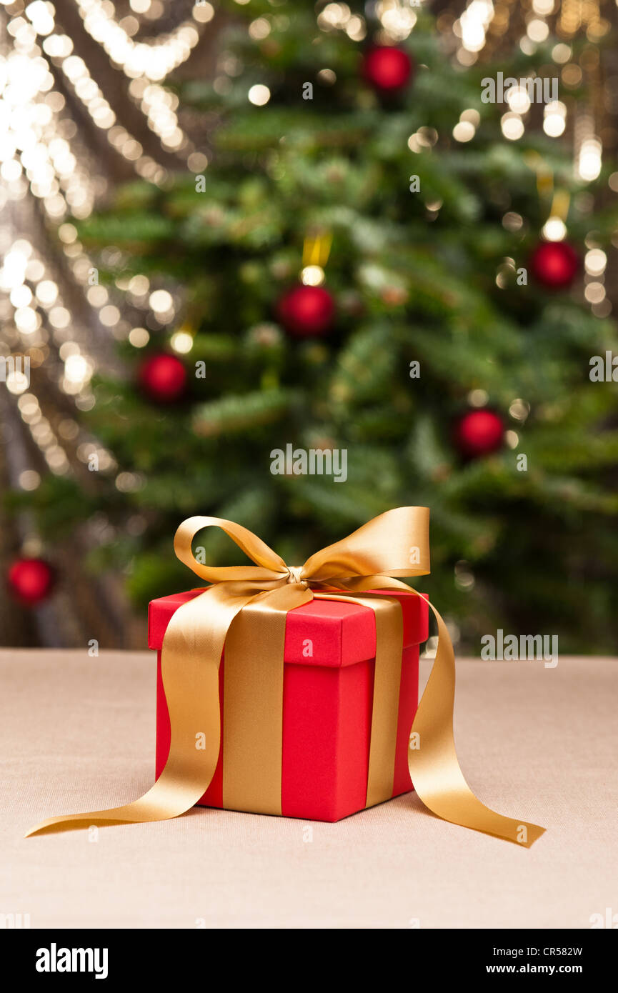 One present with gold ribbon, in front of a Christmas tree Stock Photo ...