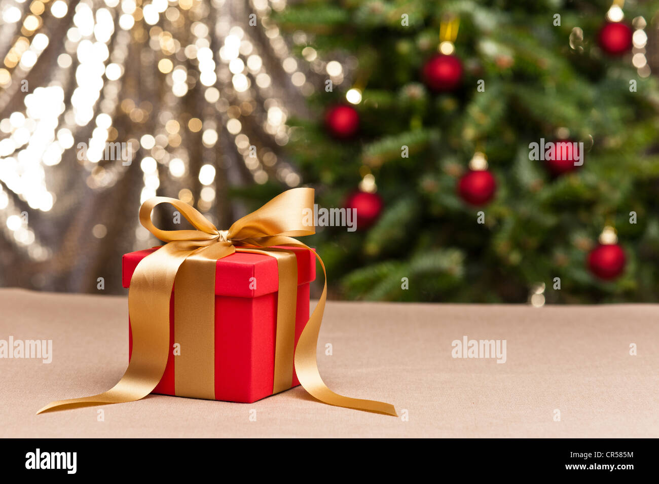 One present with gold ribbon, in front of a Christmas tree Stock Photo ...