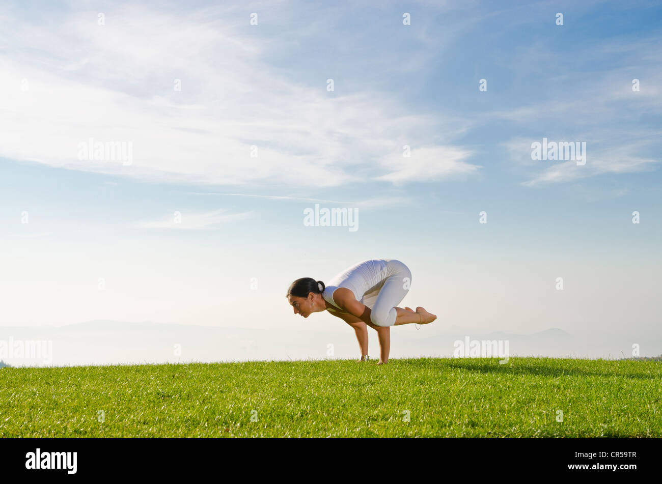 Young woman practising Hatha yoga outdoors, showing the pose kakasana ...