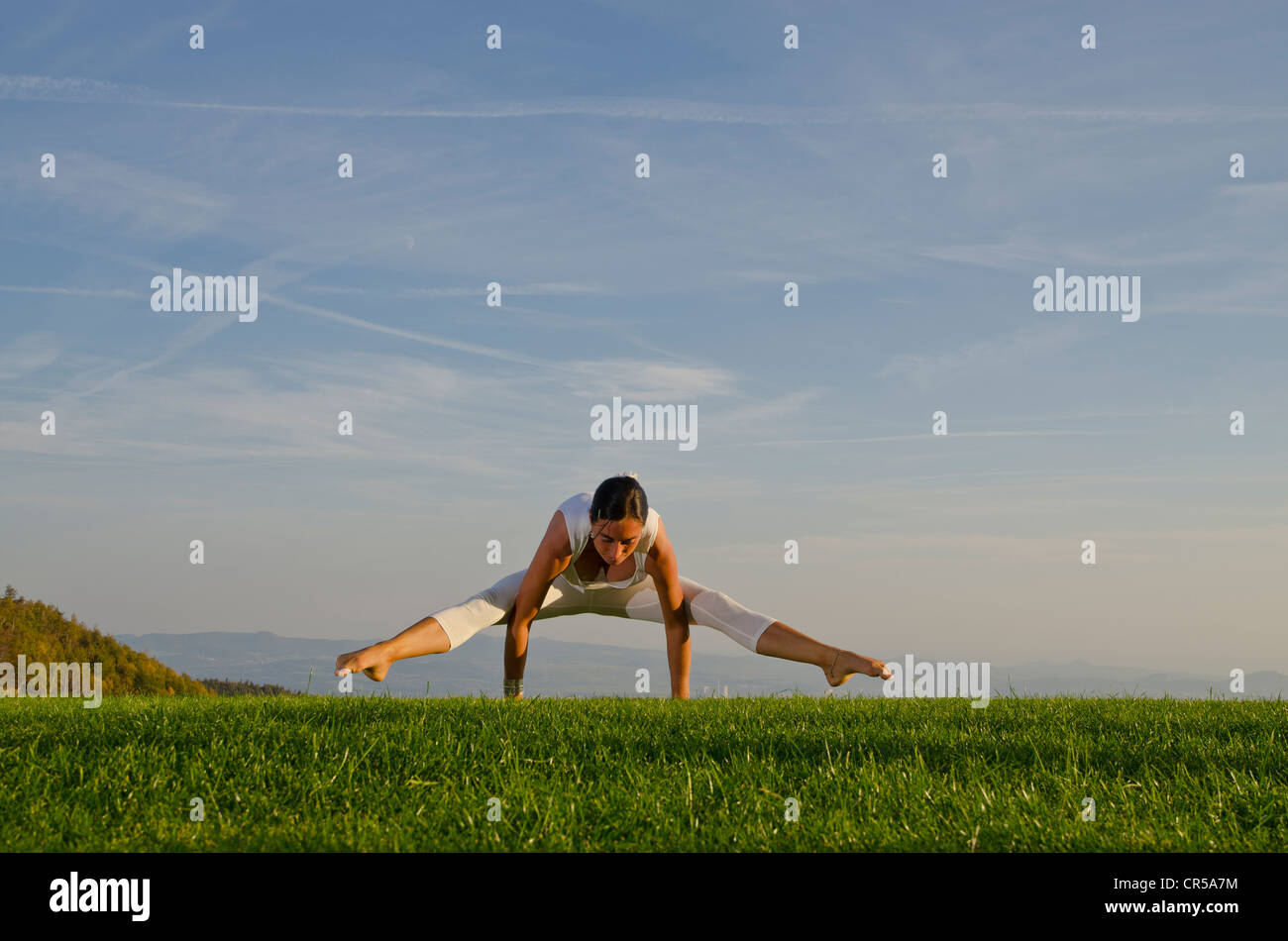 Young woman practising Hatha yoga outdoors, showing the pose kakasana ...