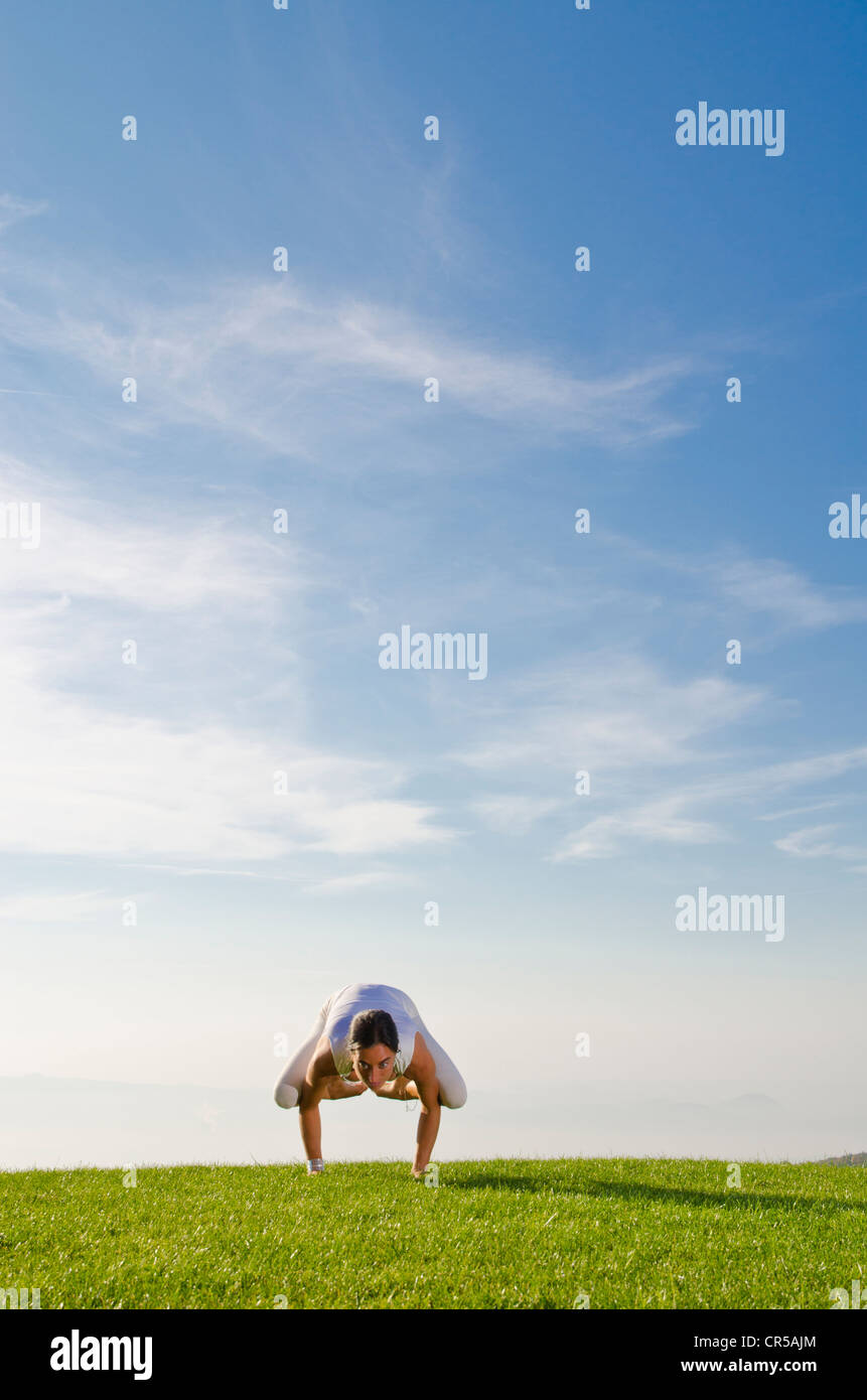 Young woman practising Hatha yoga outdoors, showing the pose kakasana ...
