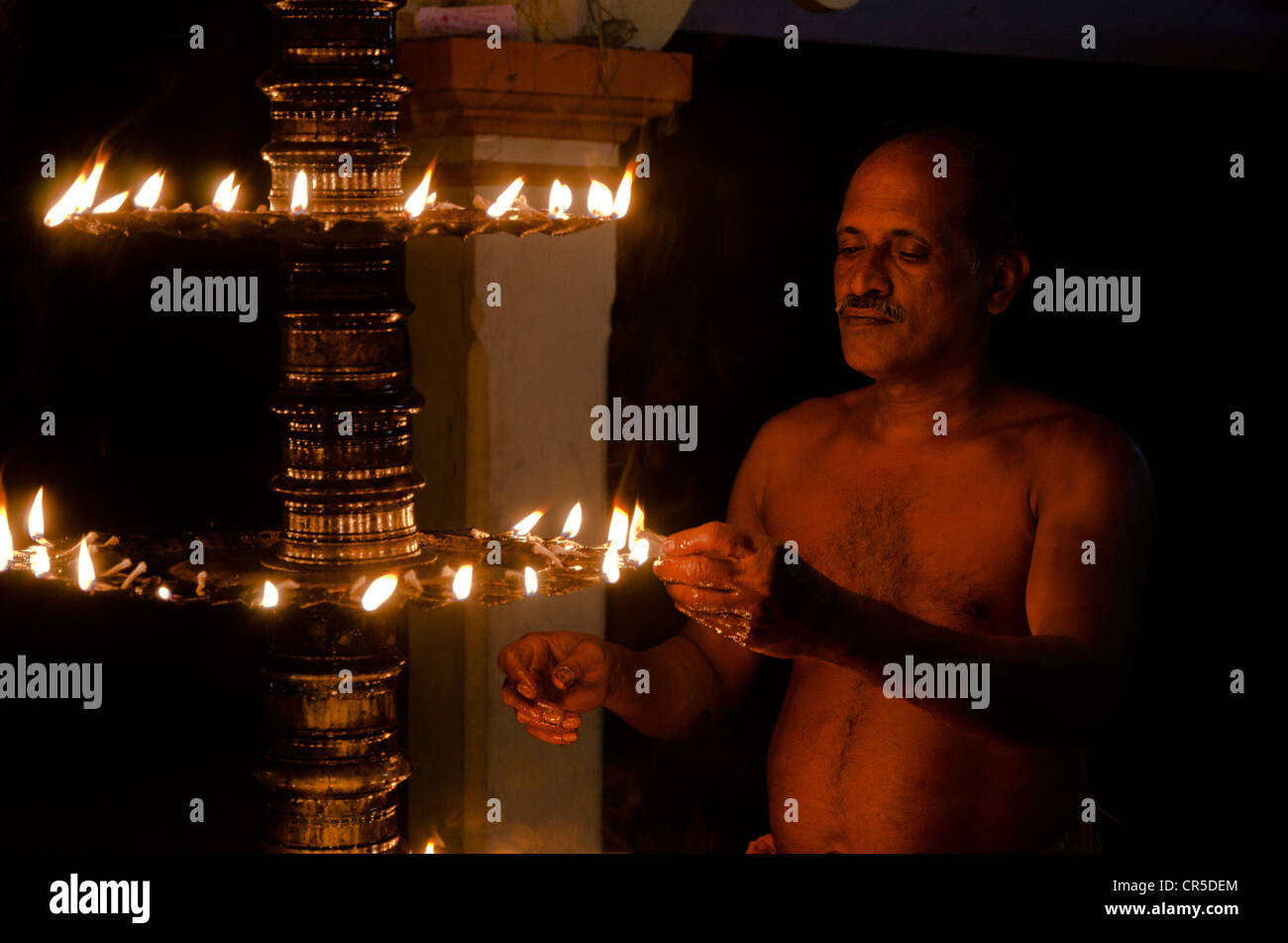 Priest is lighting little oil lamps for the evening pooja at Nagaraja ...