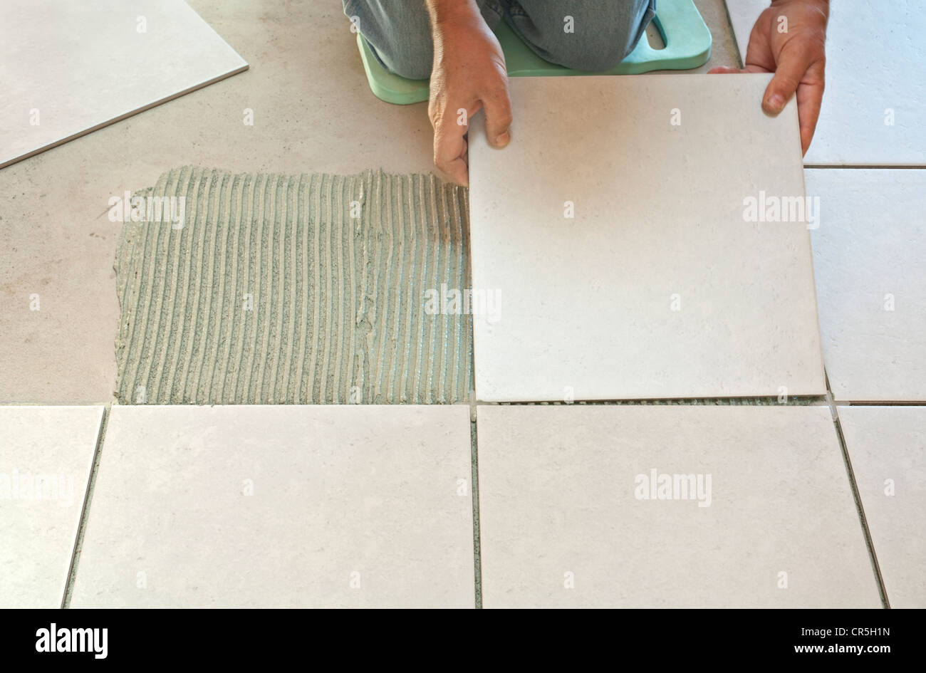 Man placing ceramic floor tile in position over adhesive Stock Photo ...