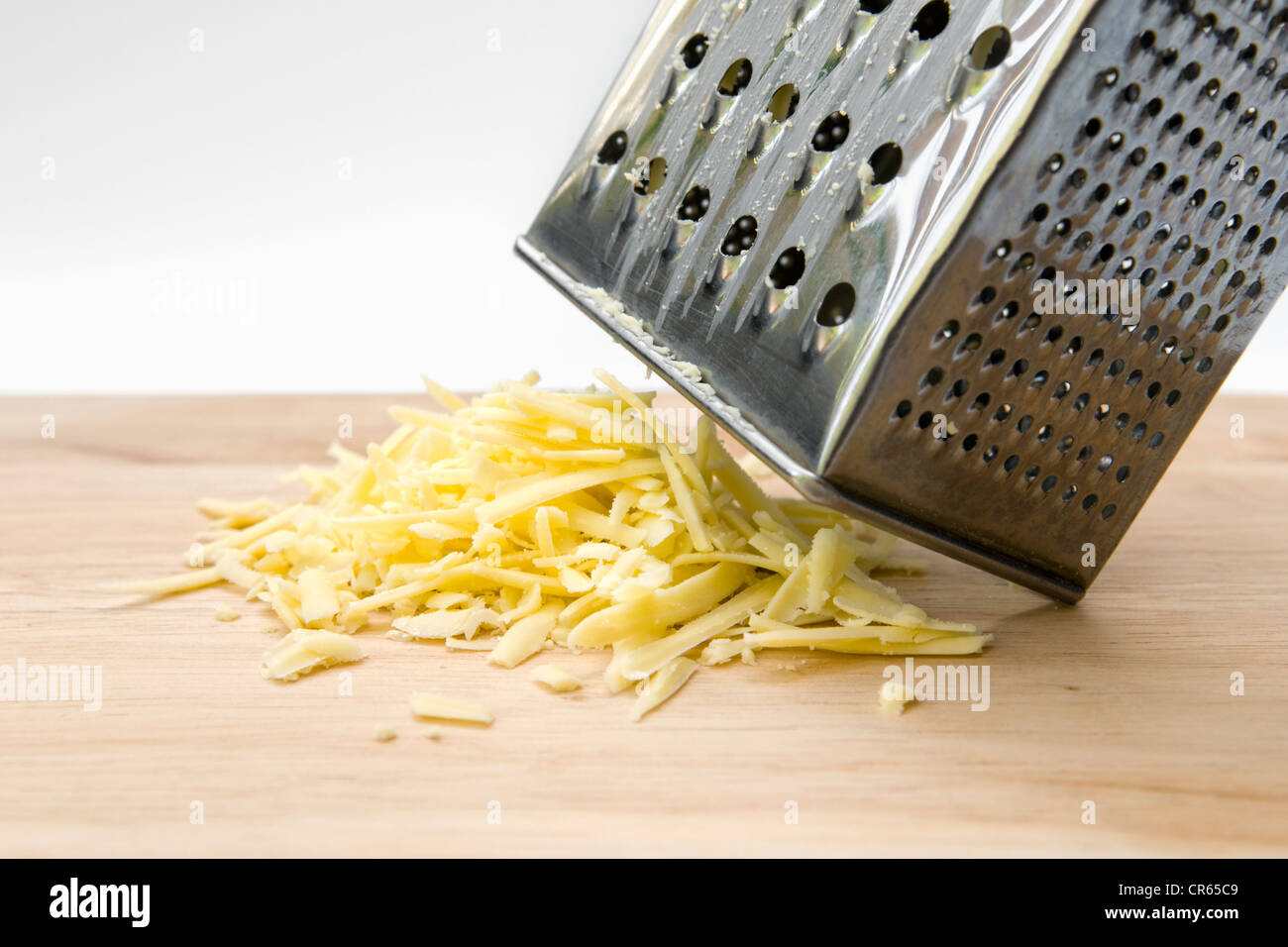 Grated cheese with grater on wooden chopping board against white ...